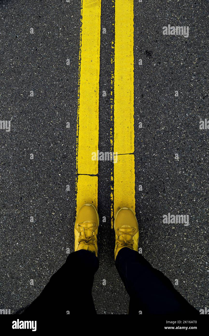 The feet of a person wearing a yellow sneaker on the yellow lines of ...