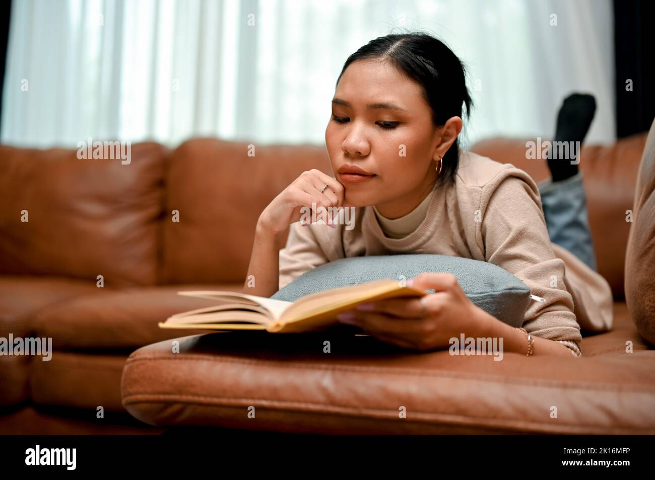Relaxed and chill young Asian female reading a book or novel while ...