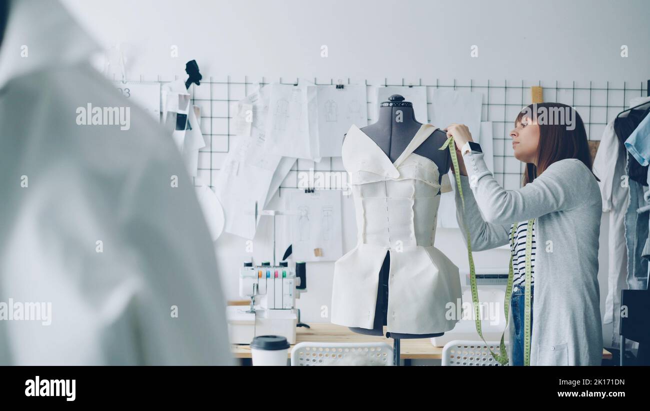 Confident pretty young woman is adjusting clothes on tailoring dummy ...