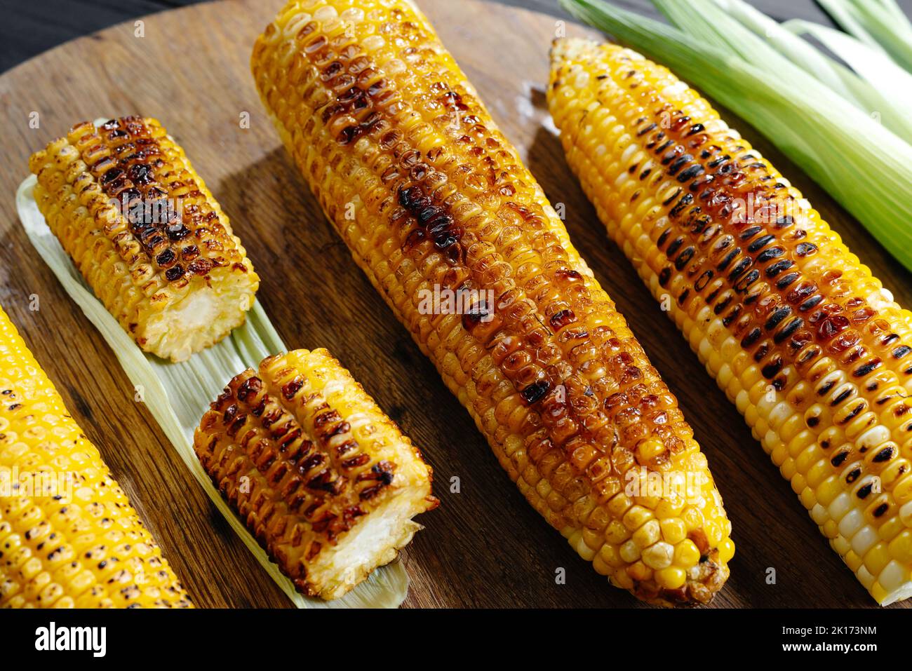 A cob of corn roasted over charcoal on a wooden board. Whole corn cobs ...
