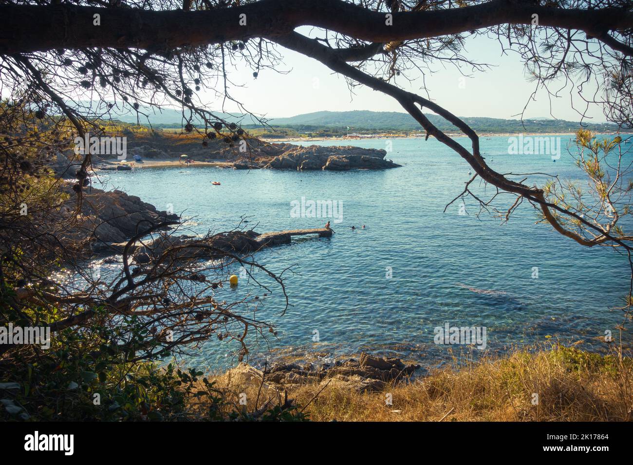 Old stone pier on small bay on French coast, beach seen through tree ...
