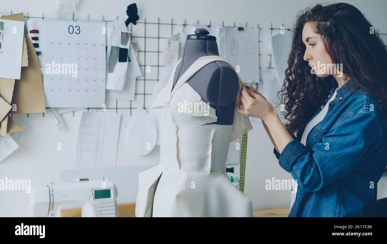 Young female tailor is adjusting clothes on tailoring dummy with sewing ...
