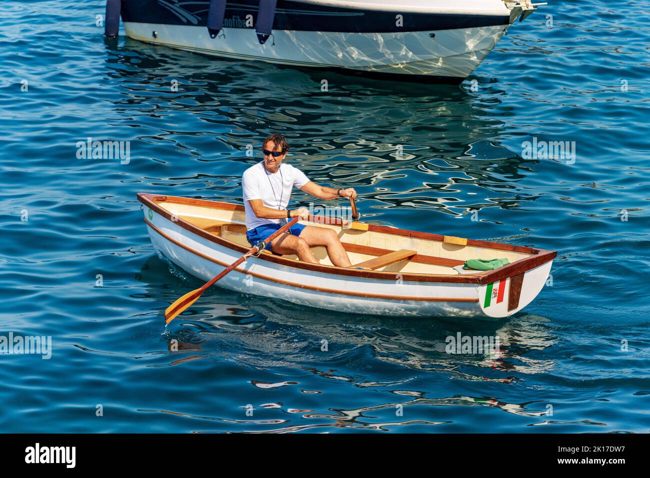 Adult man aboard of a small white and brown wooden rowing boat in the ...