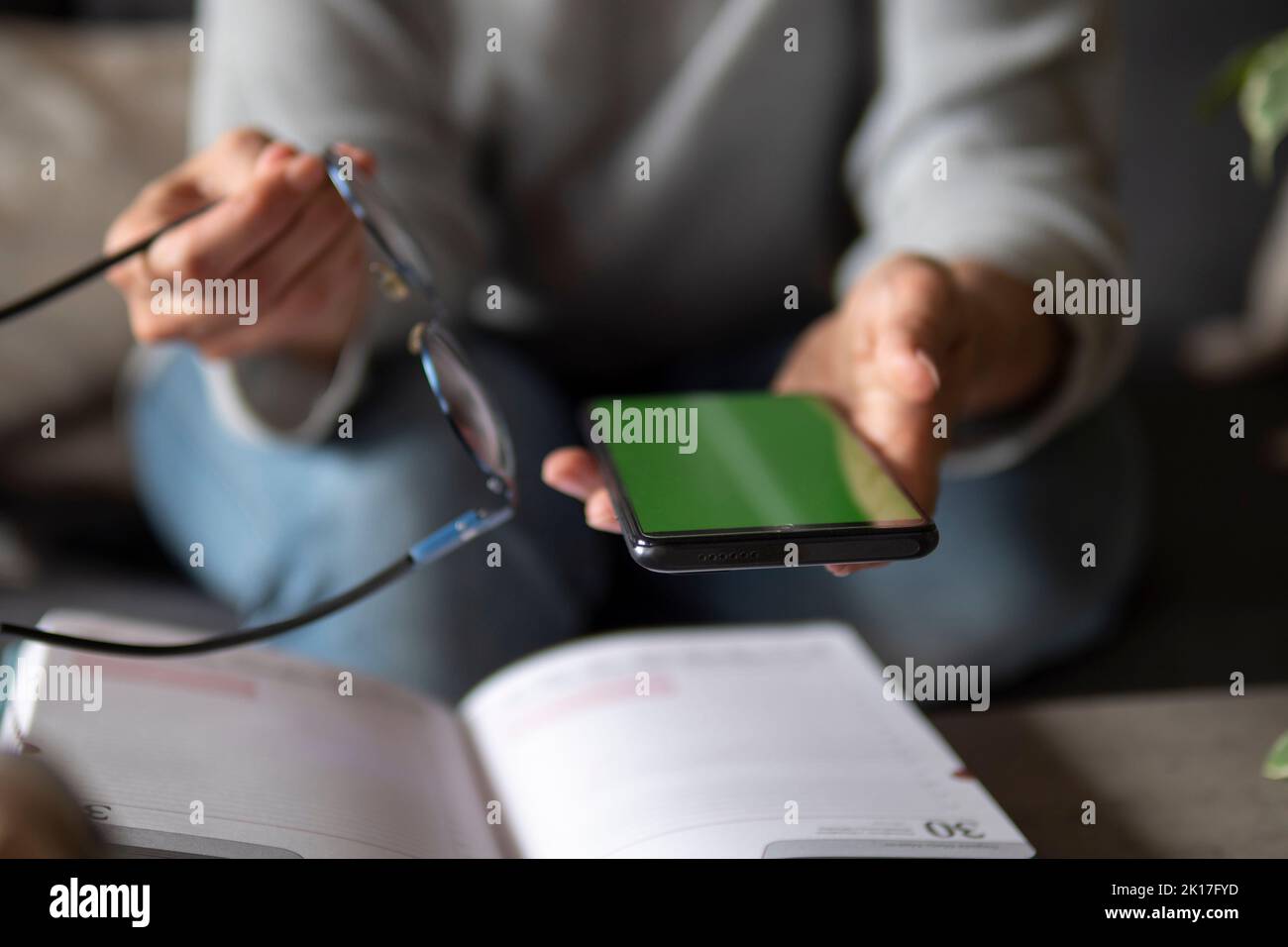 Female hand holding smartphone with green screen. Woman sitting on sofa ...