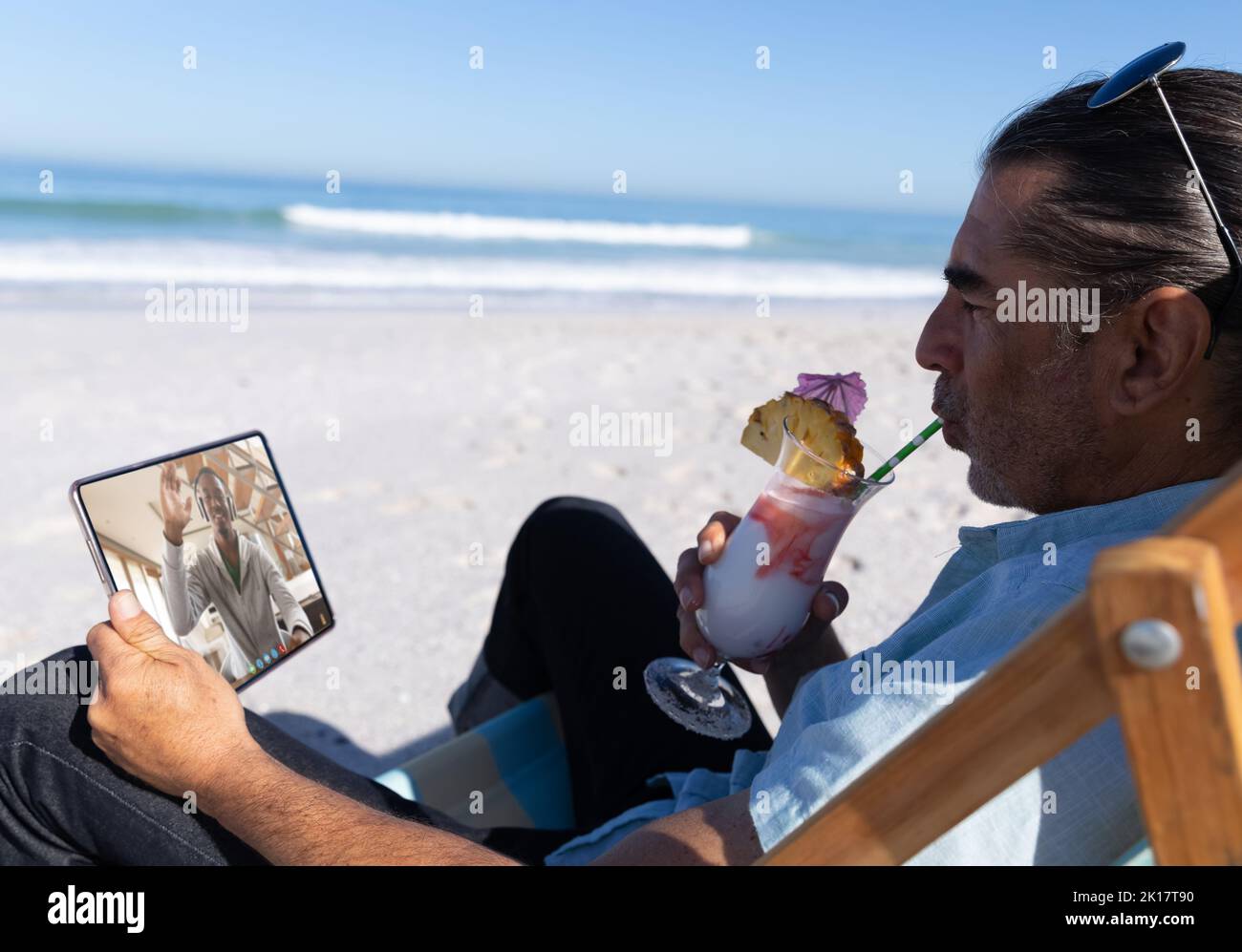 Caucasian man relaxing on beach with drink having video call using ...