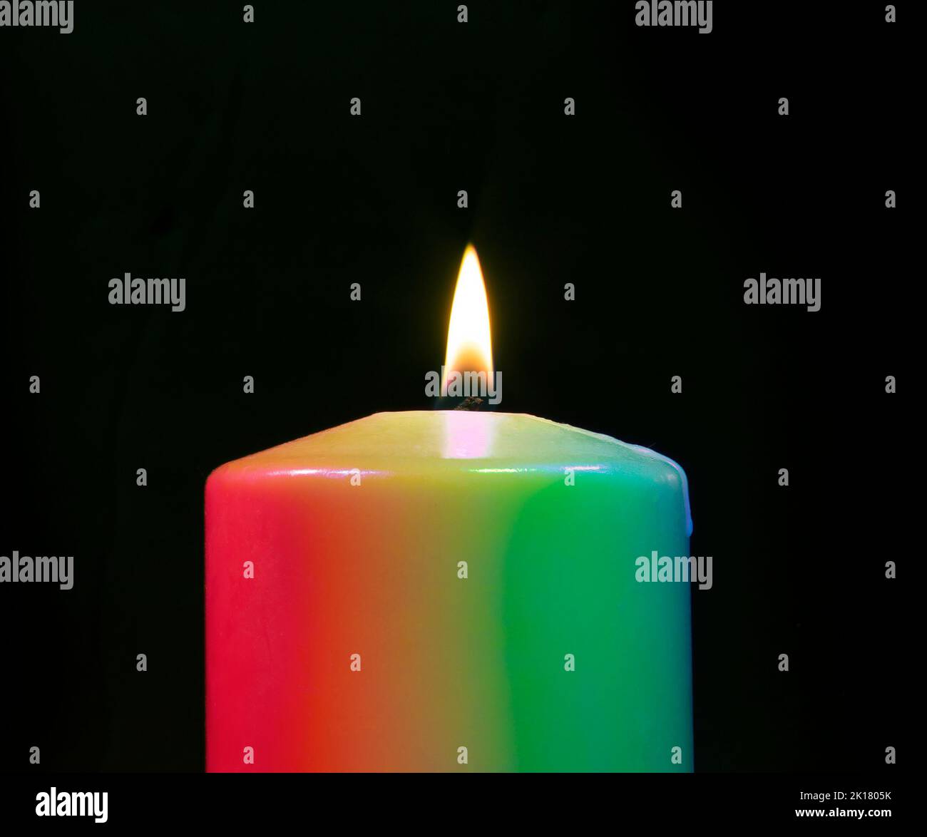 Rainbow candle burning on a black background with wax just strating to ...