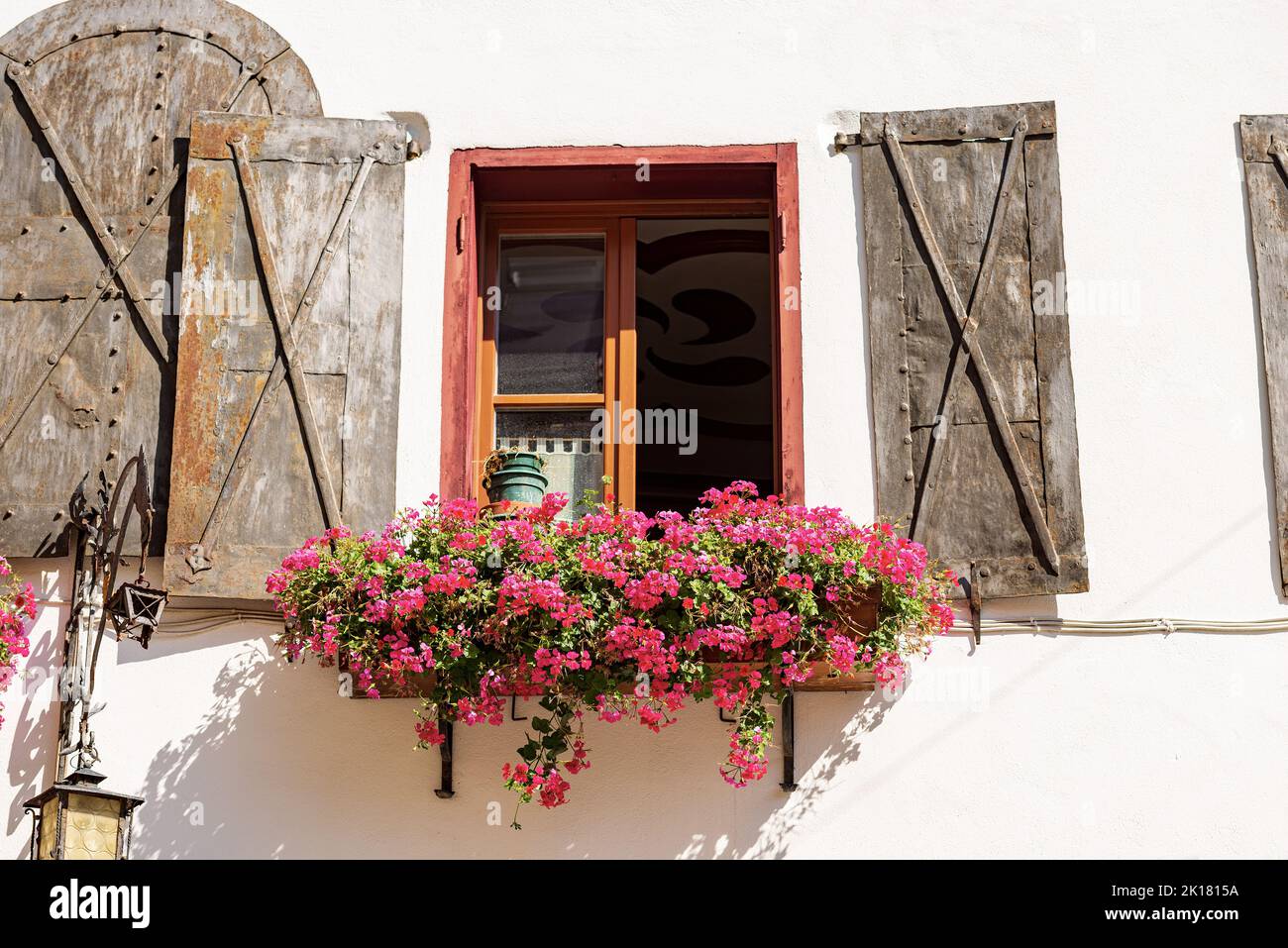 Ancient window with metal shutters and red geranium flowers. Small ...