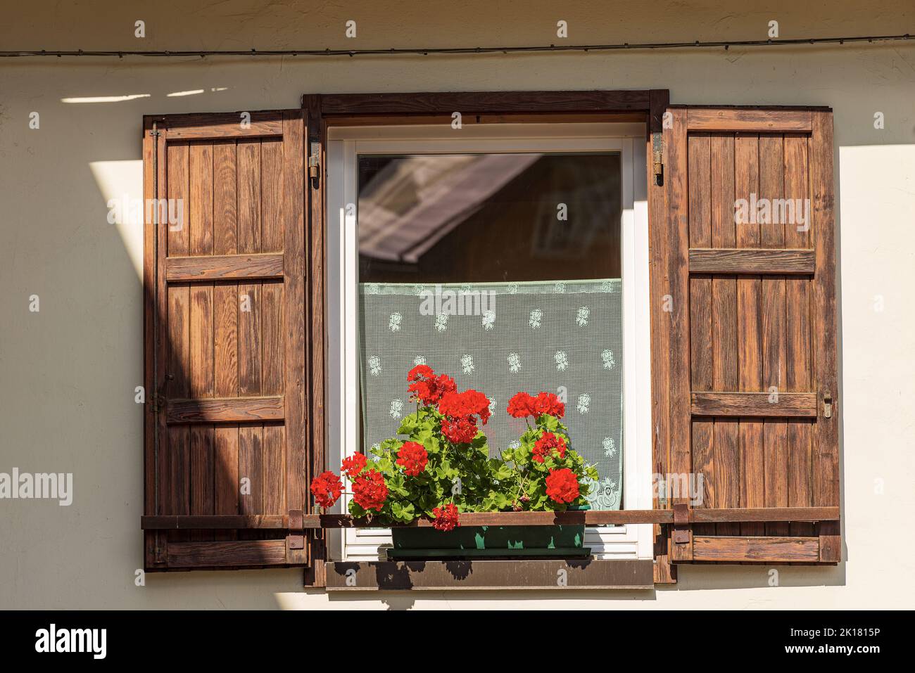 Window with wooden shutters and red geranium flowers. Small village of ...