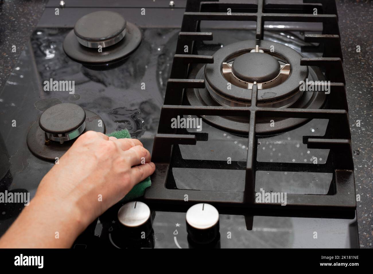 A housewife cleans the kitchen gas glass-ceramic black stove with a ...
