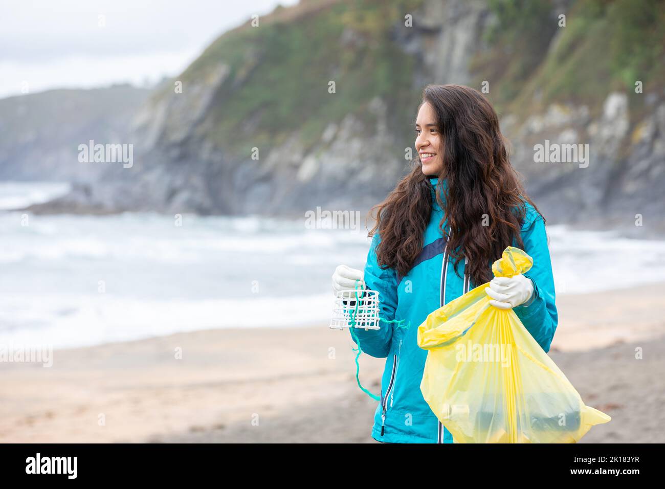 Smiling Hispanic lady standing near ocean and cleaning up beach from ...