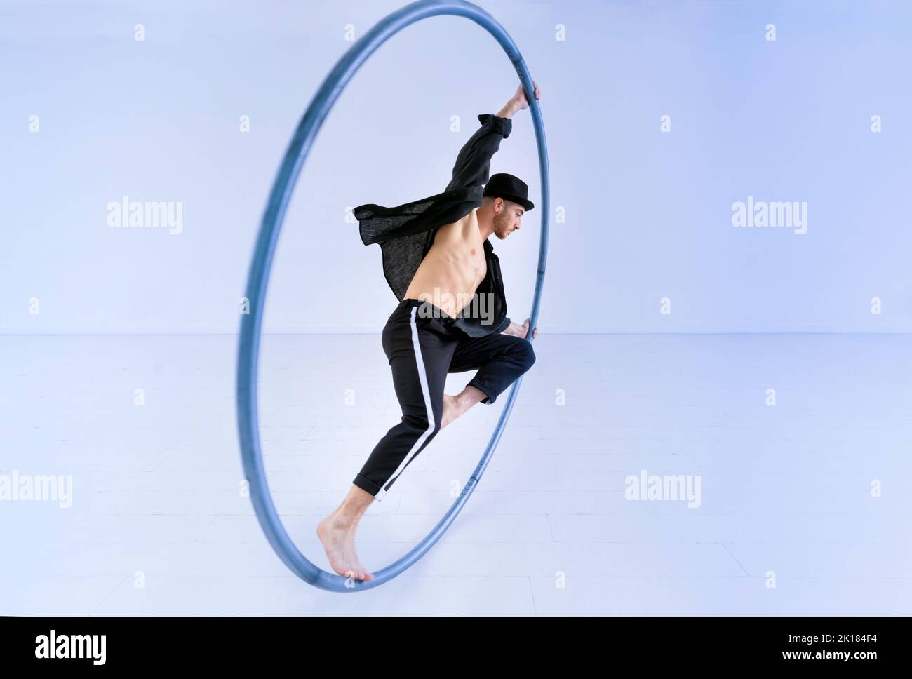 Full body barefoot man in costume doing trick on cyr wheel against blue ...