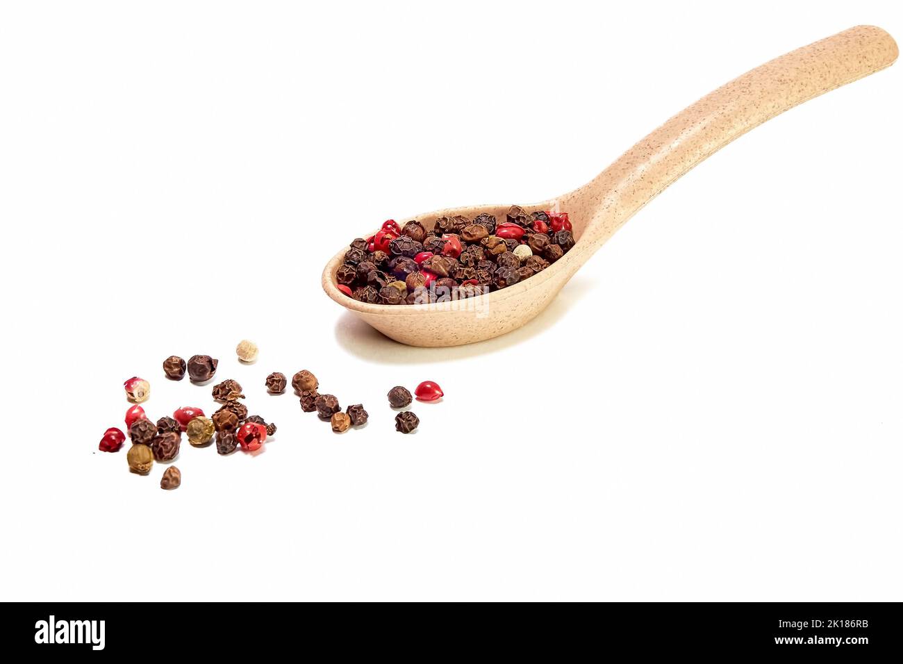 Mixture of peppers in a wooden spoon on a white background, seasonings ...