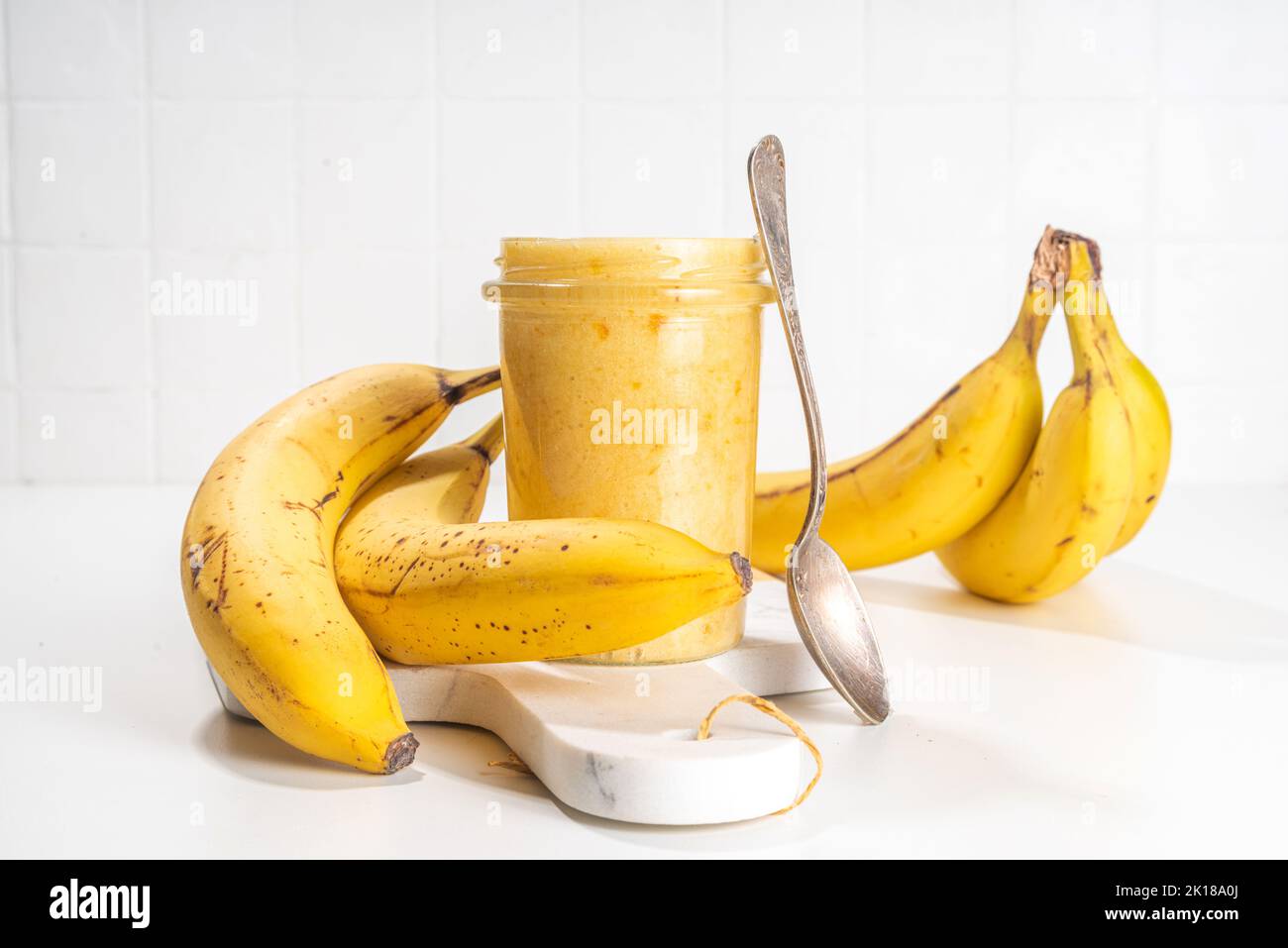 Bananas jam in small glass jar with fresh bananas on white table ...