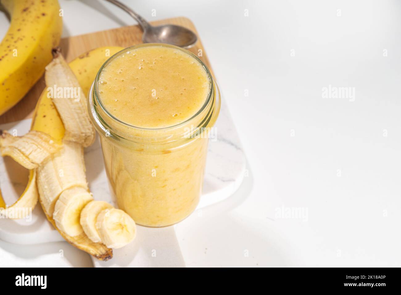 Bananas jam in small glass jar with fresh bananas on white table ...