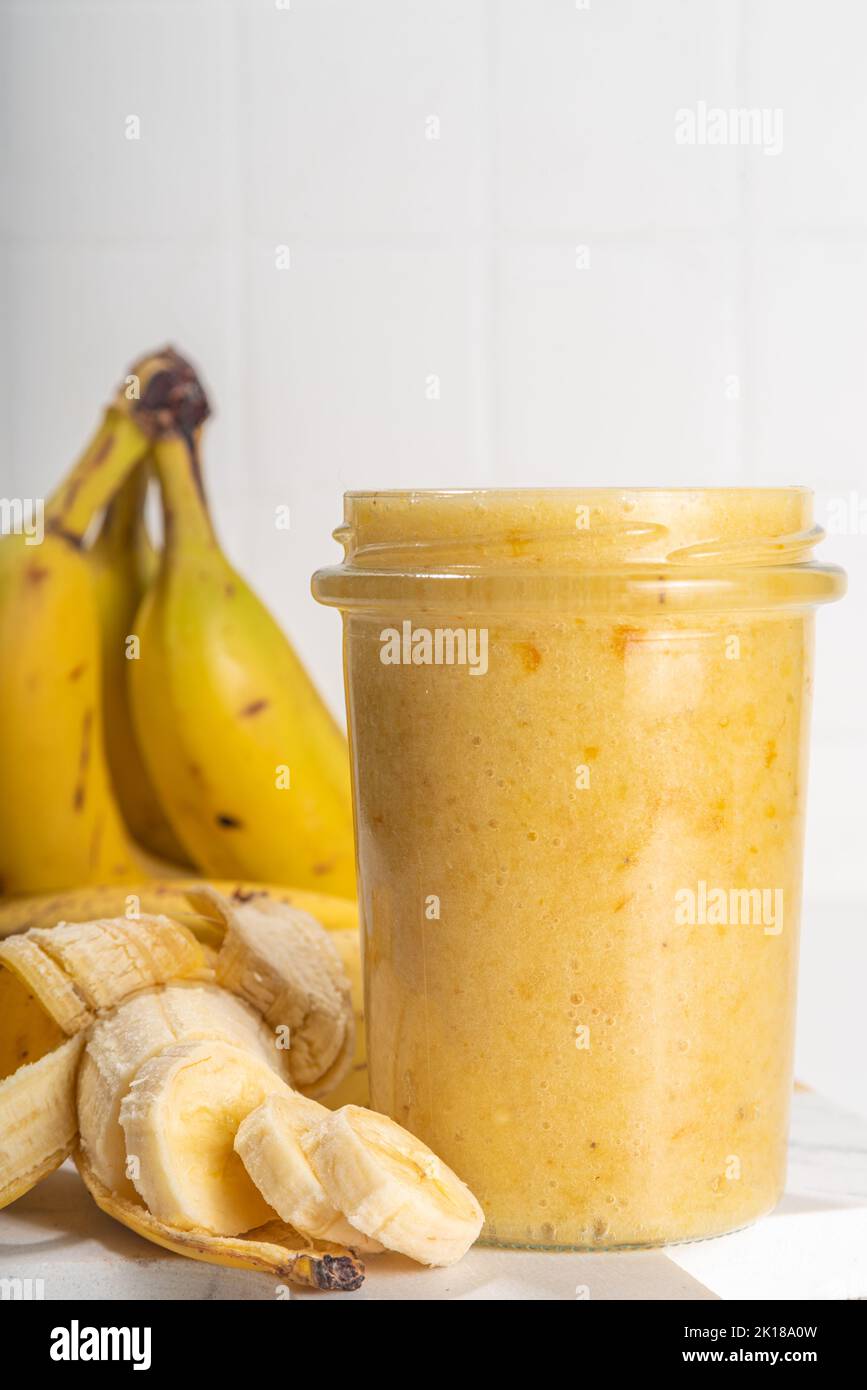 Bananas jam in small glass jar with fresh bananas on white table ...