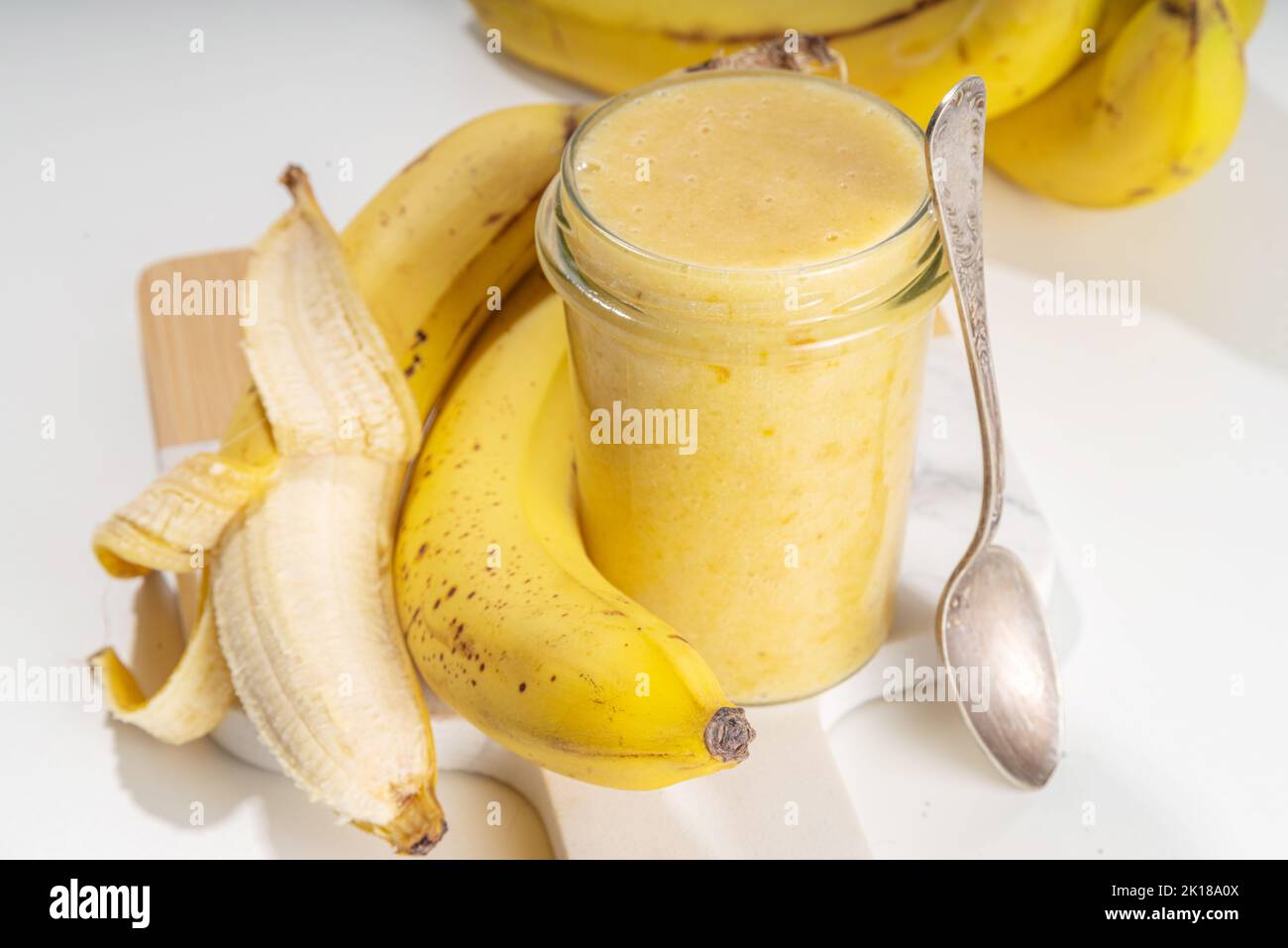Bananas jam in small glass jar with fresh bananas on white table ...