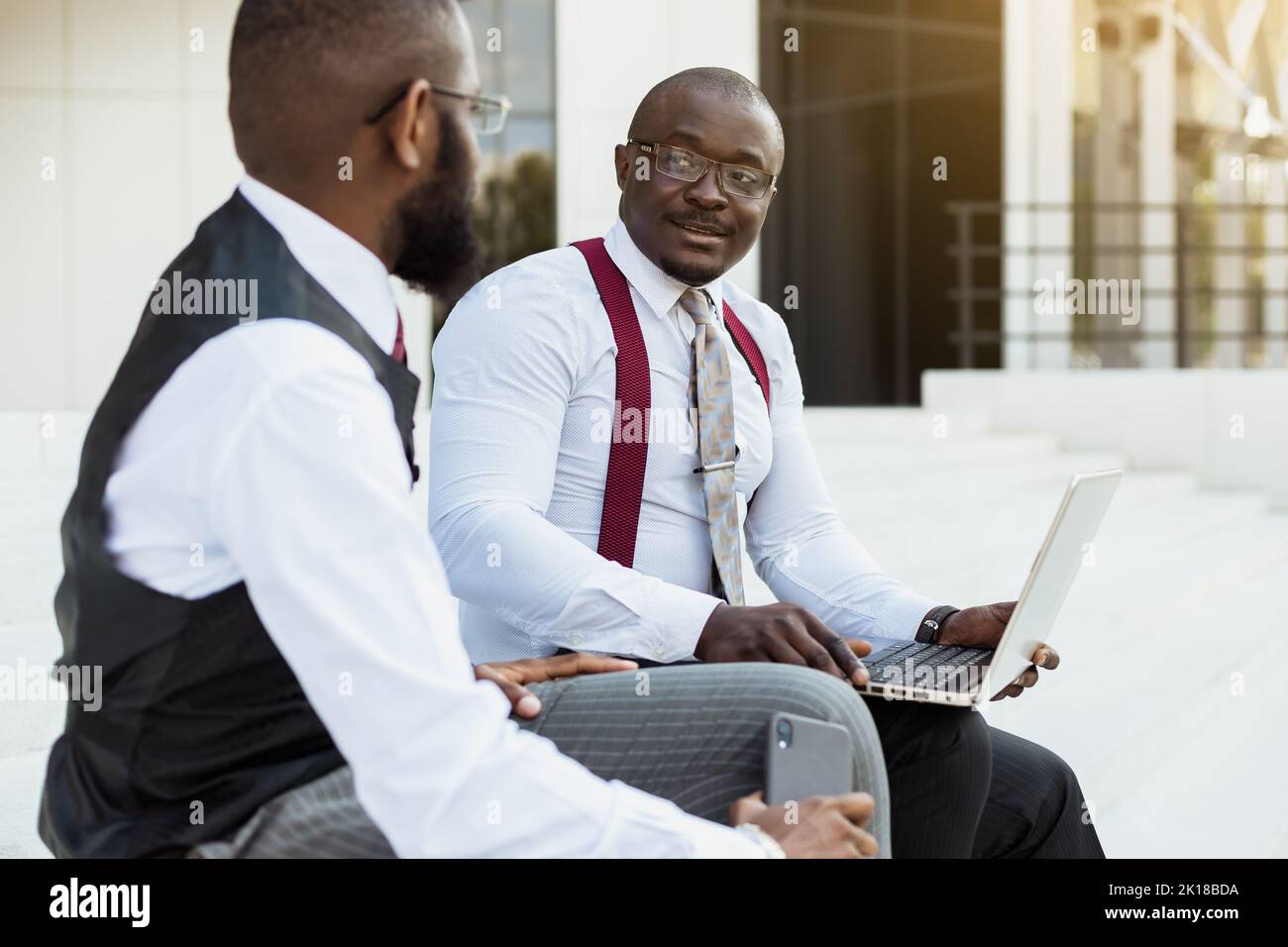 Business meeting outdoors. Two dark-skinned men in suits sit on the ...
