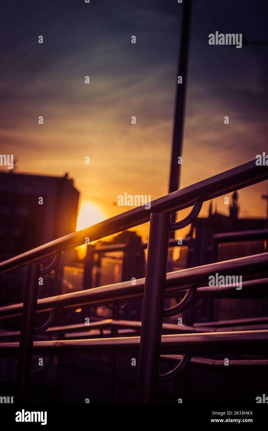 A vertical dramatic shot of a bright sunset behind a metallic fence ...