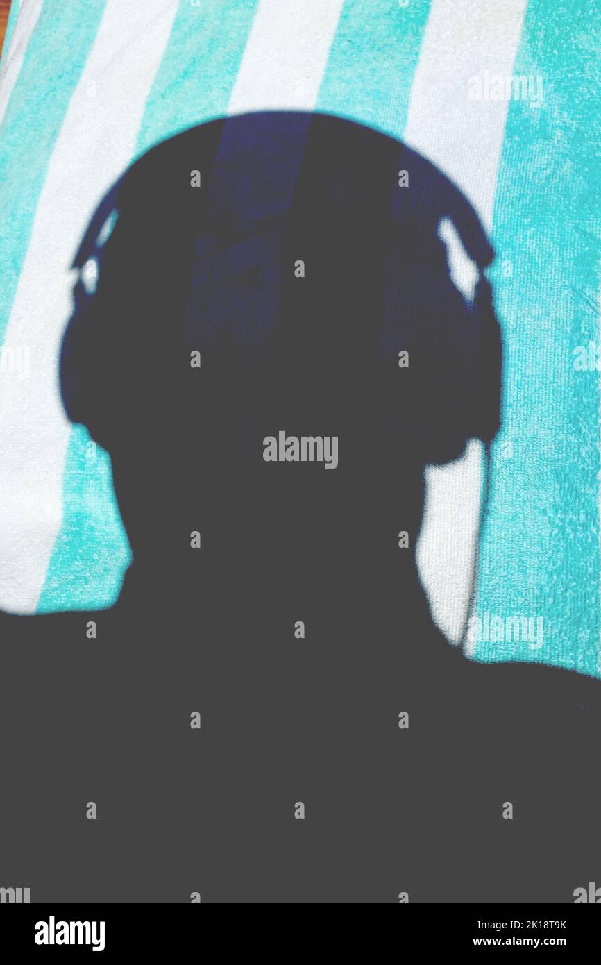Shadow cast on a beach towel of a man wearing headphones to represent ...
