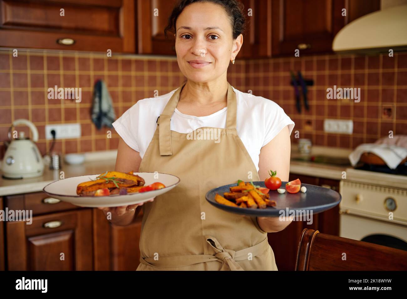 Charming multi-ethnic woman in beige chef's apron carrying served ...