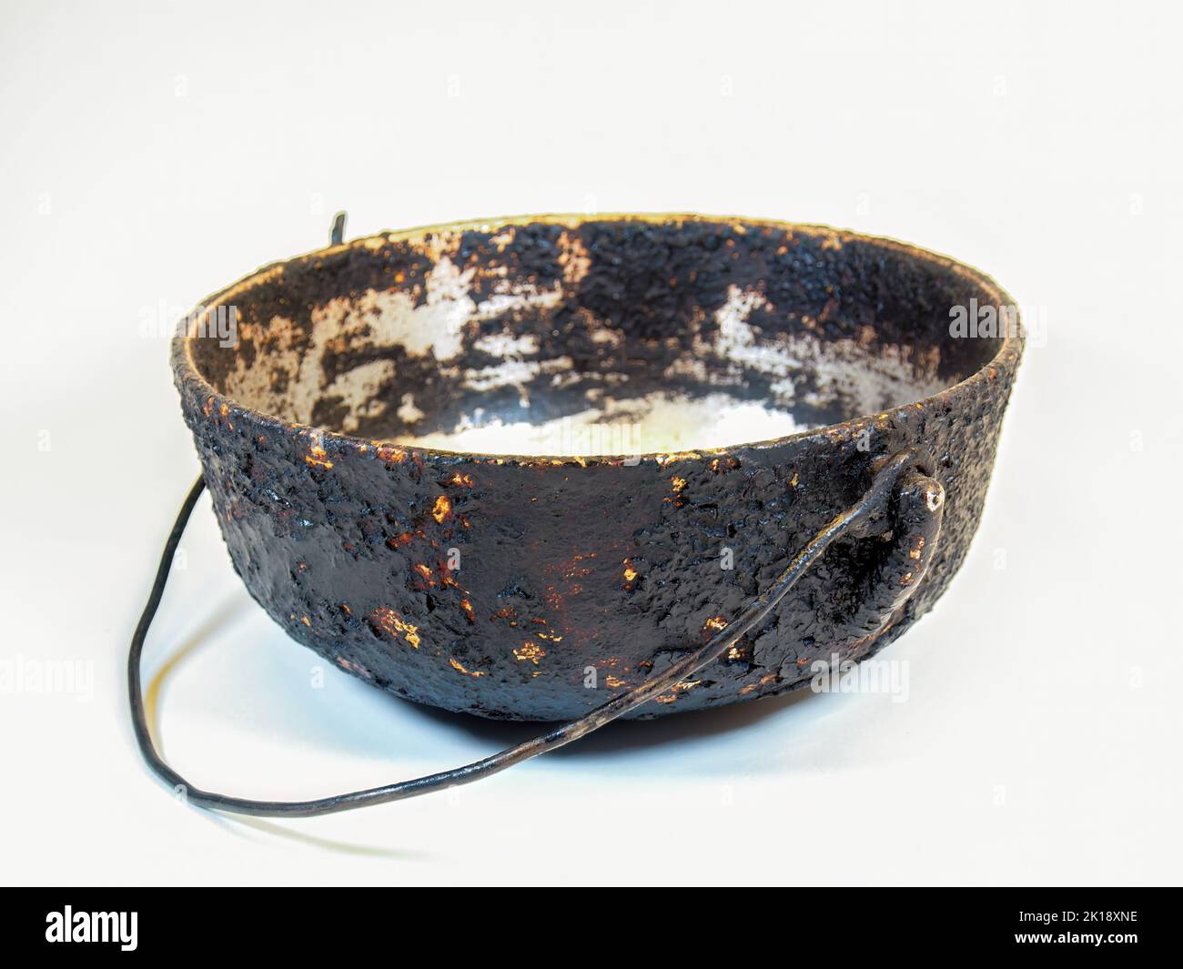Studio shot of a very battered, burnt and old metalic pot on a neutral ...