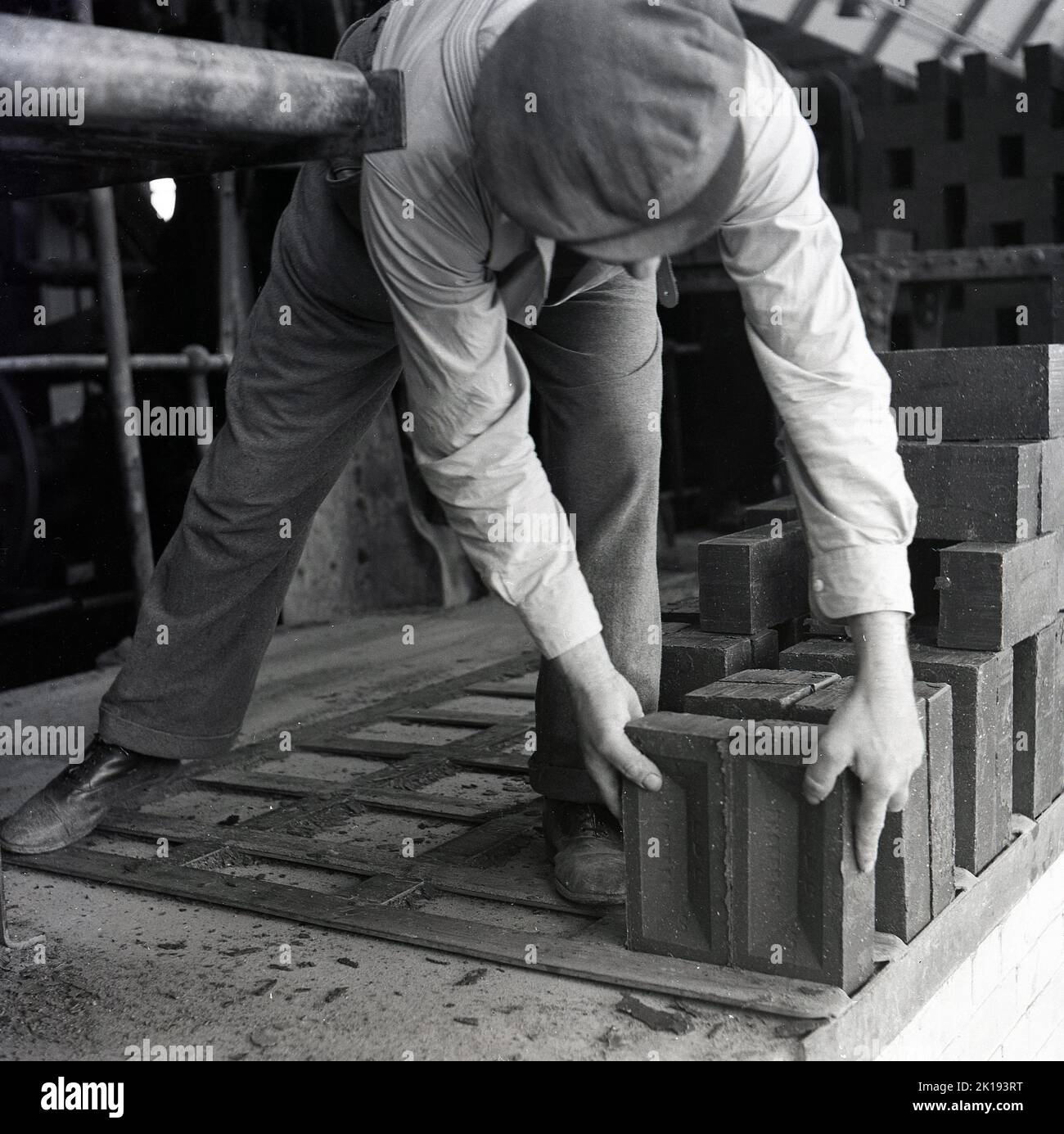 1950s, historical, a male worker, wearing a flat cap, stacking newly fired bricks at the London ...