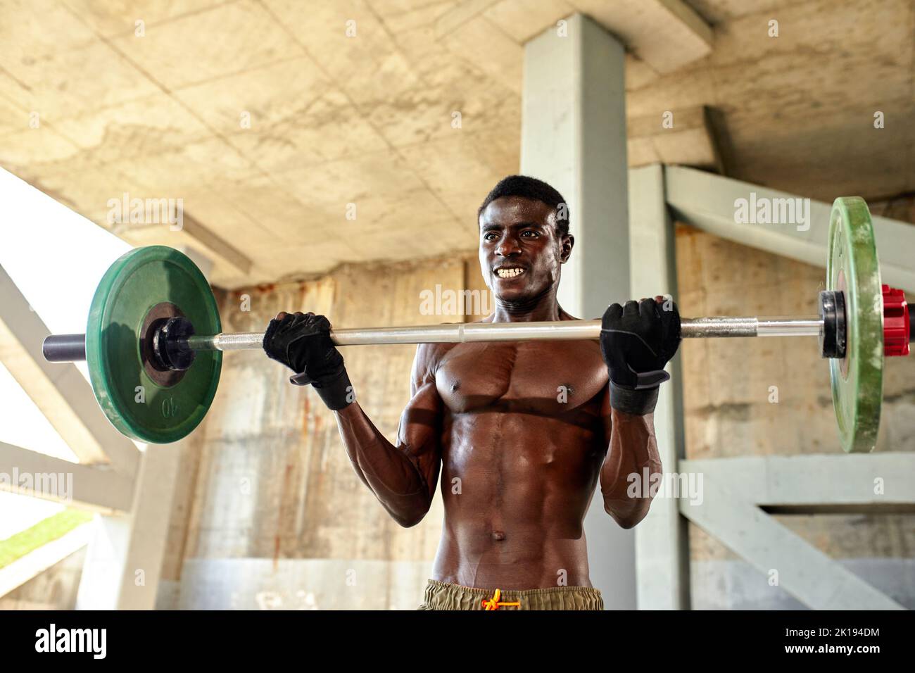 Athletic black young man lifting a heavy-weight barbell in outdoor gym ...