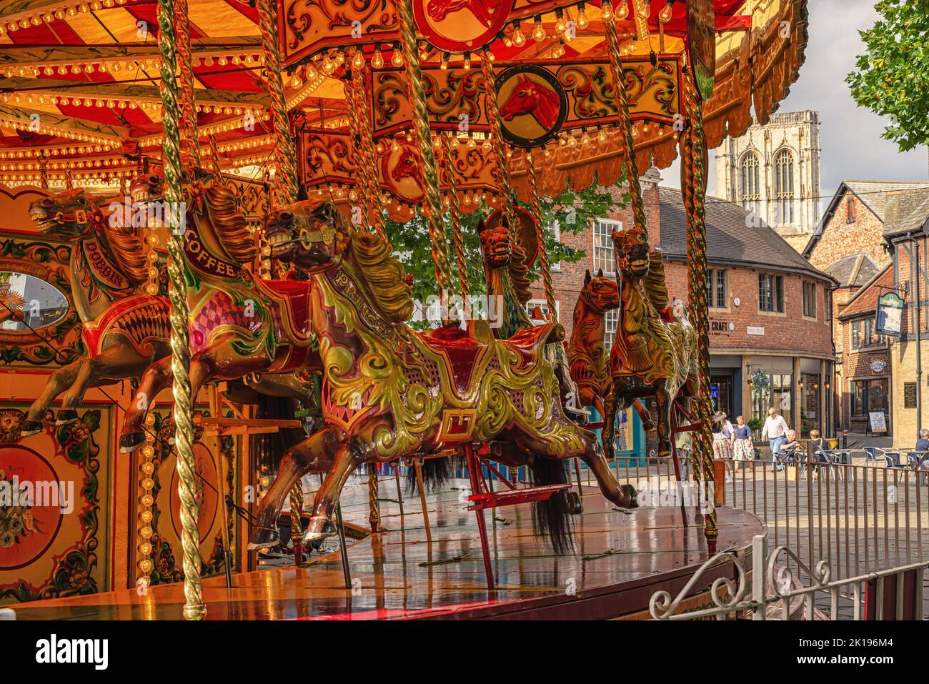 A colourful carousel with horses are set in a town square with historic ...