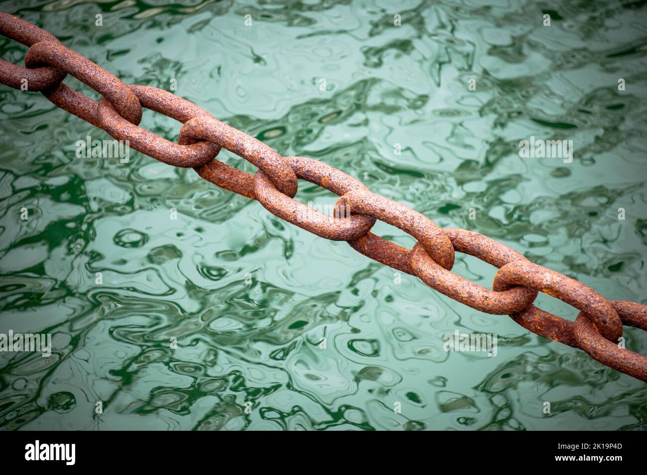 Rusted maritime anchor chain stretched taut over green harbor waters ...