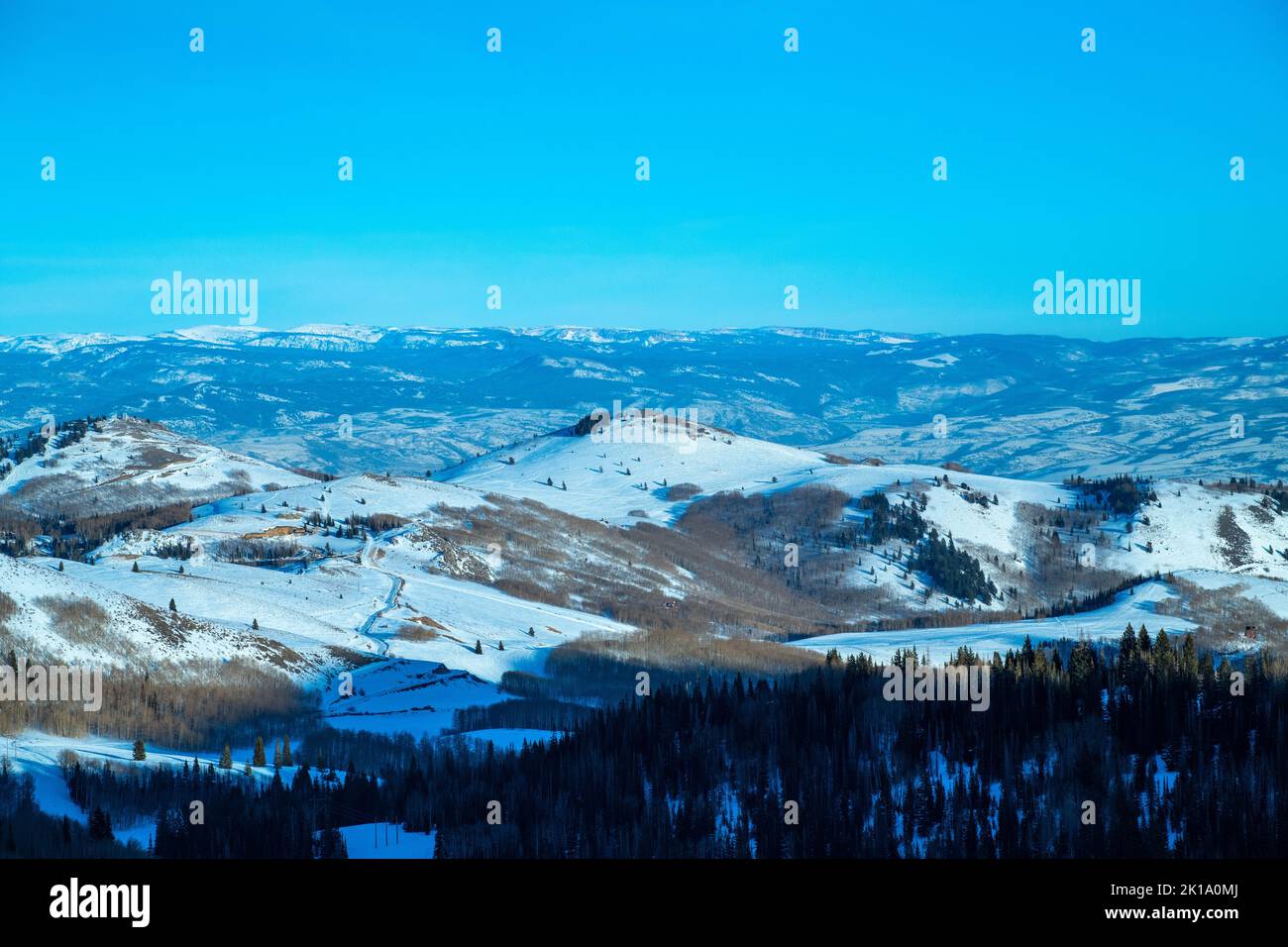 A drone view of snowy hills and mountains under sunlight with forests ...