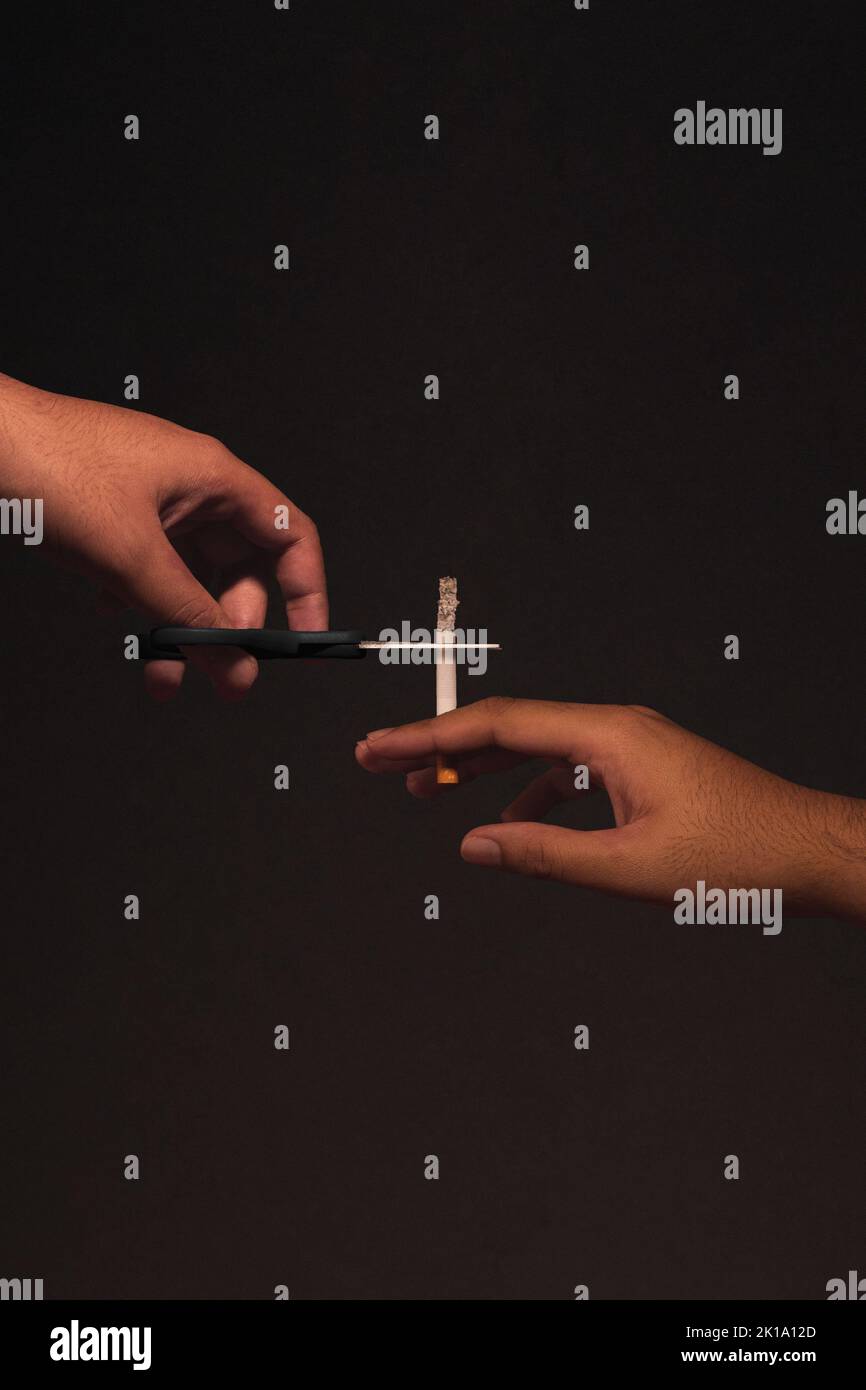 A human hand cutting with scissors a cigarette in another human hand ...