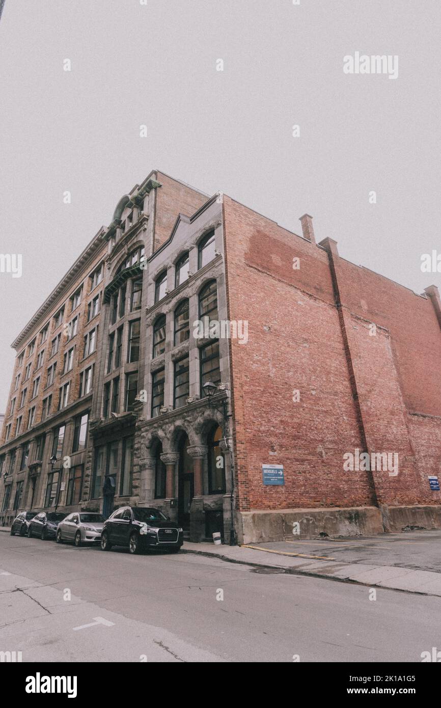 A vertical shot of a brick building with parked cars by a sidewalk ...