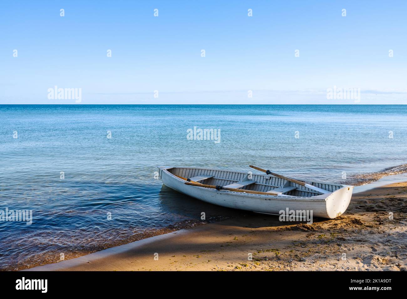 Old row boat on beach with shadow of trees. Calm ocean on the horizon ...
