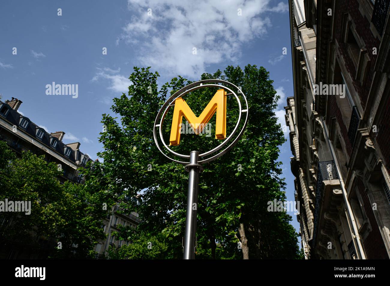 Sign with the subway logo (yellow symbol) in front of a parisian metro ...