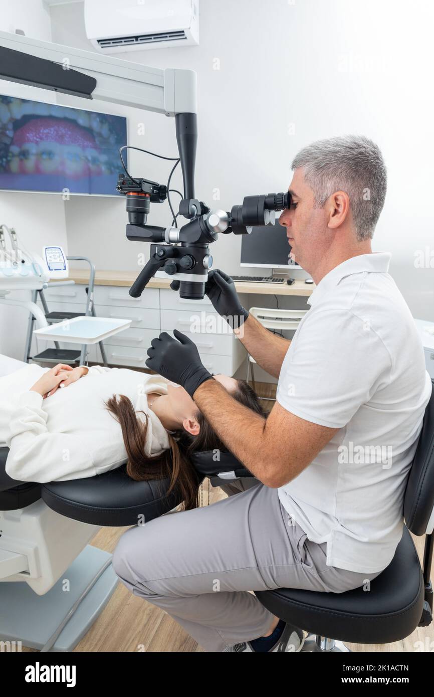 Dentist using dental microscope treating patient dental clinic office ...