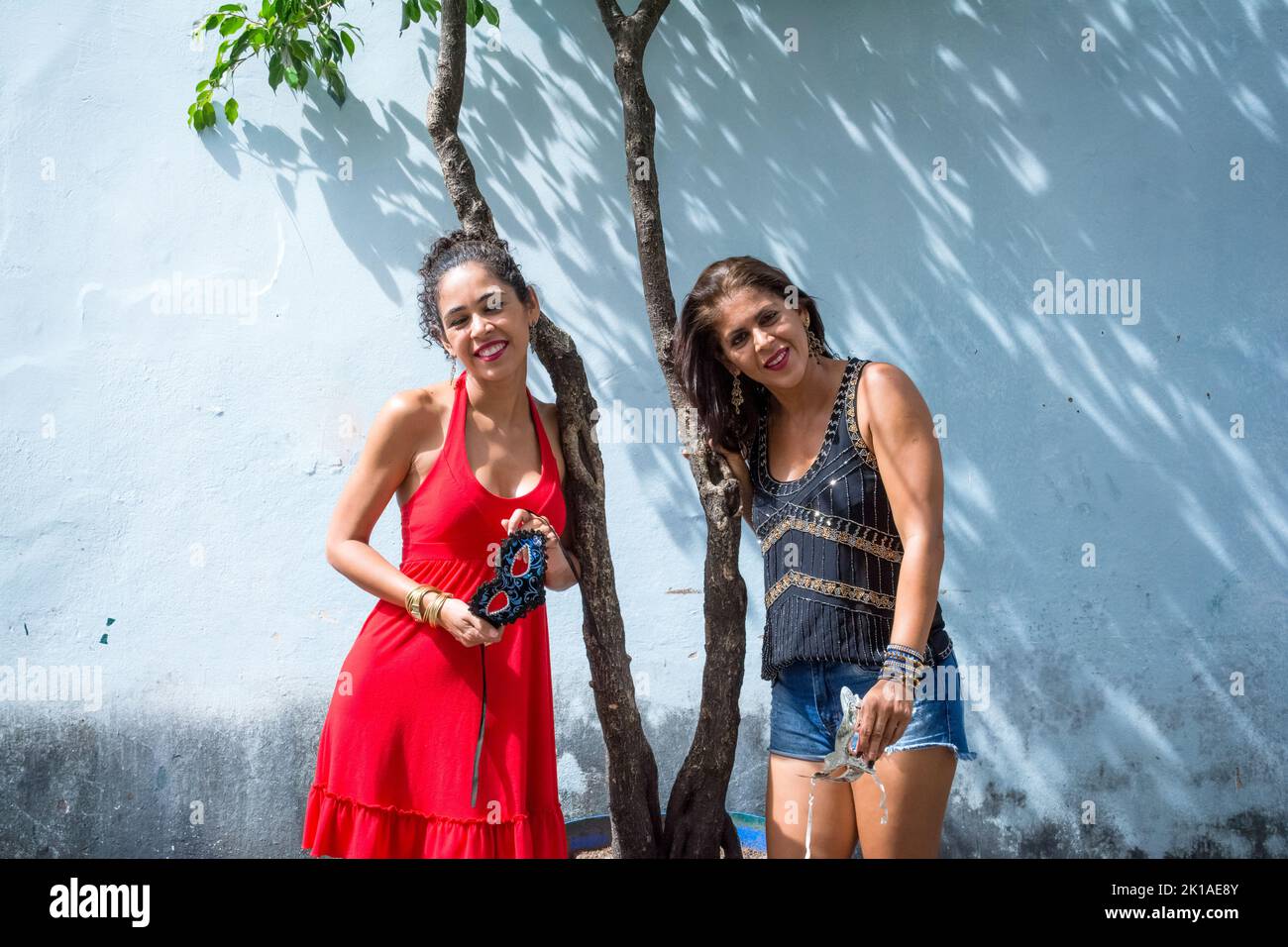 Portrait of two girls between a tree branch against a light blue wall ...