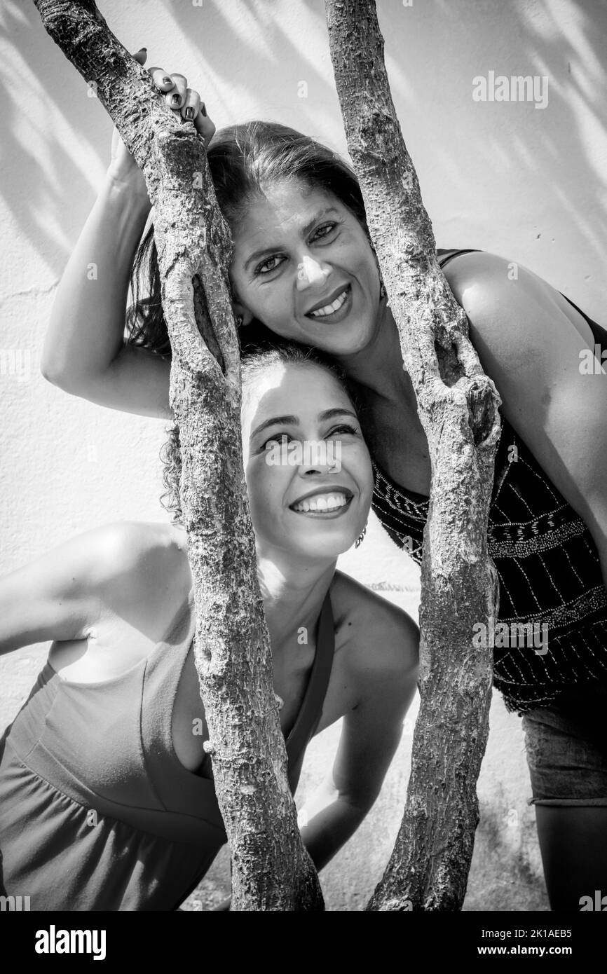 Portrait of two girls between a tree branch against a light blue wall ...
