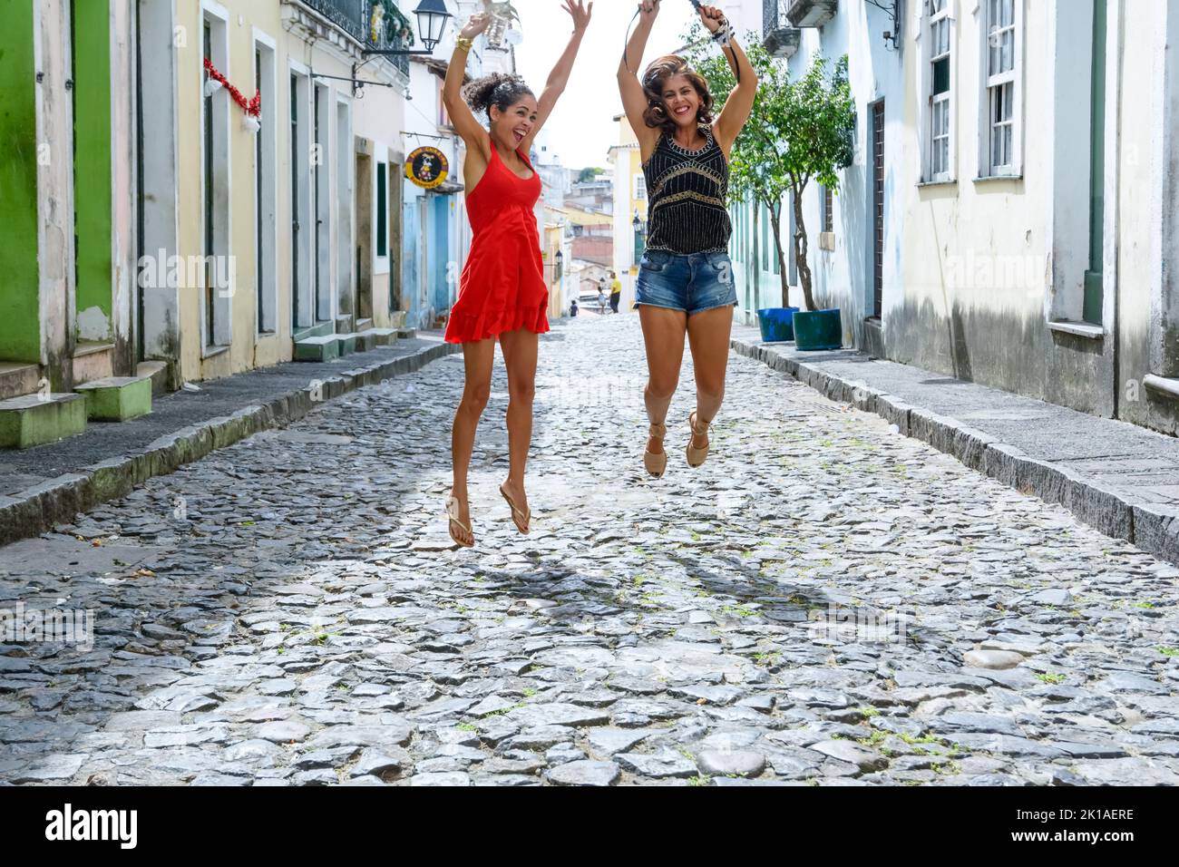 Portrait of two beautiful and happy girls jumping on the cobblestone ...