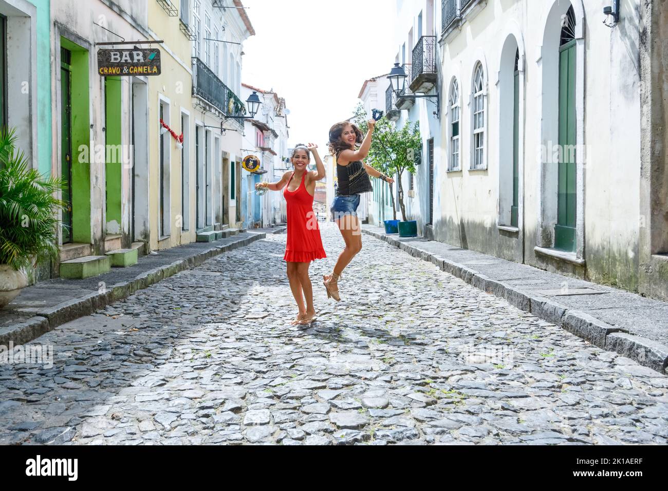 Portrait of two beautiful and happy girls jumping on the cobblestone ...