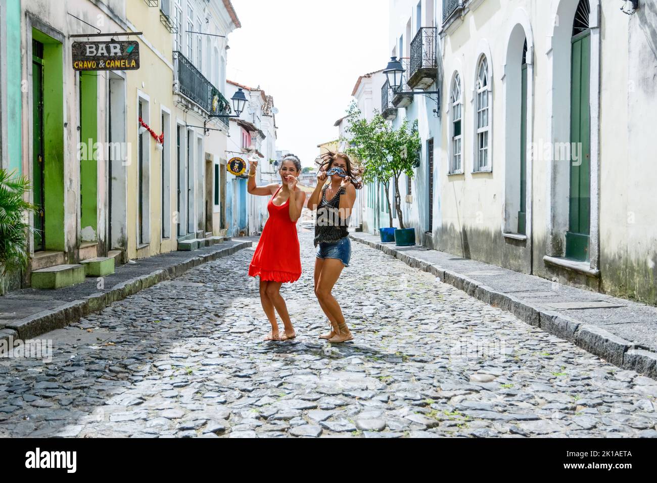 Portrait of two beautiful and happy girls jumping on the cobblestone ...