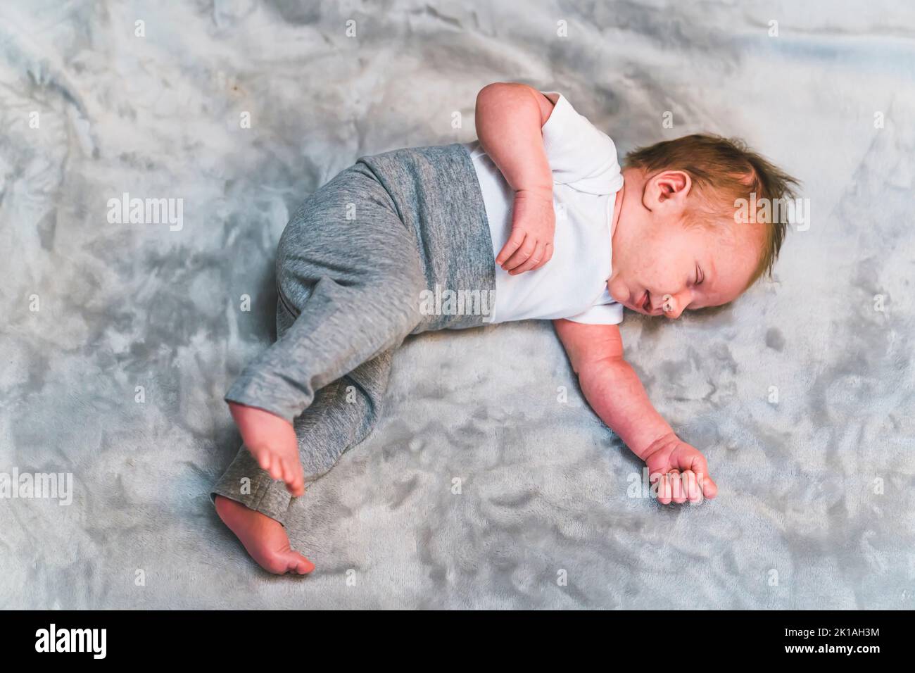 An infant baby boy with cute brown hair, laying on his side back on a ...