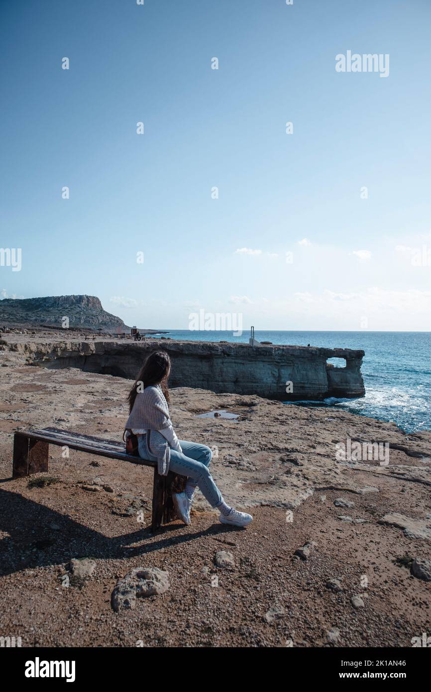 Young woman is sitting on a bench and looking at sea caves near cape ...