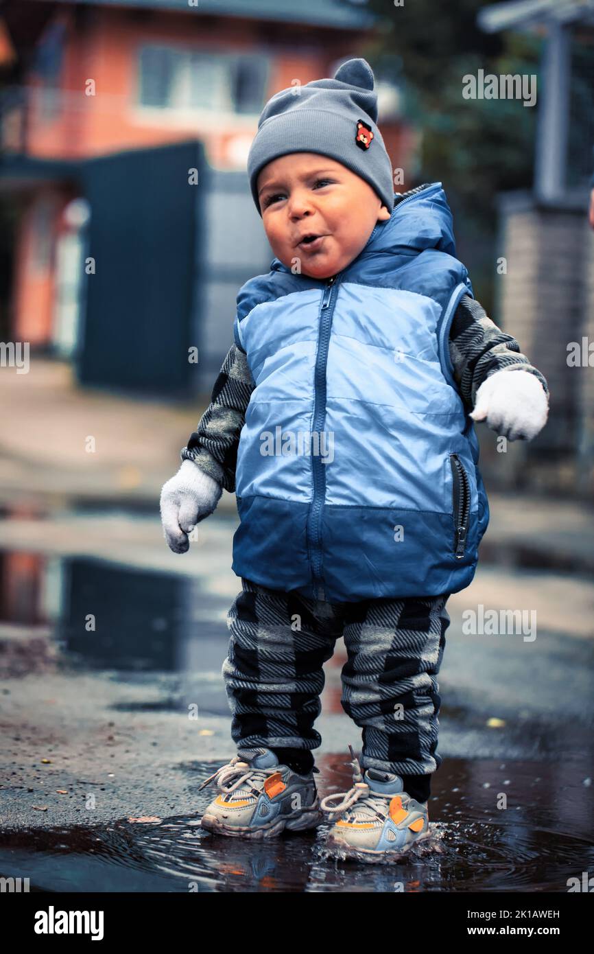 little boy jumps in puddles. Splashes of water fly in different ...