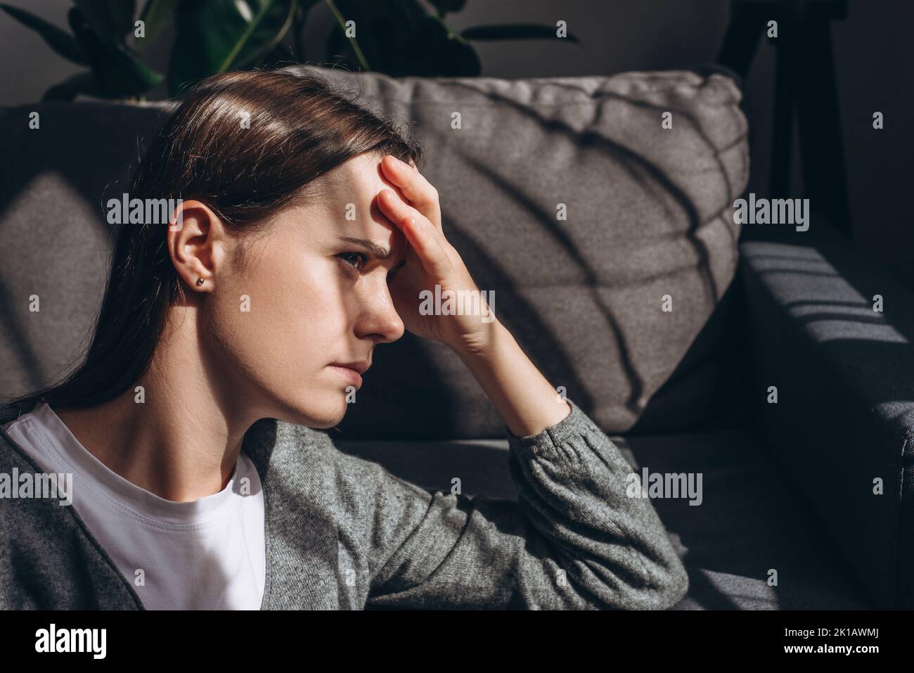 Close up of worried young woman sit on couch at home look in distance ...