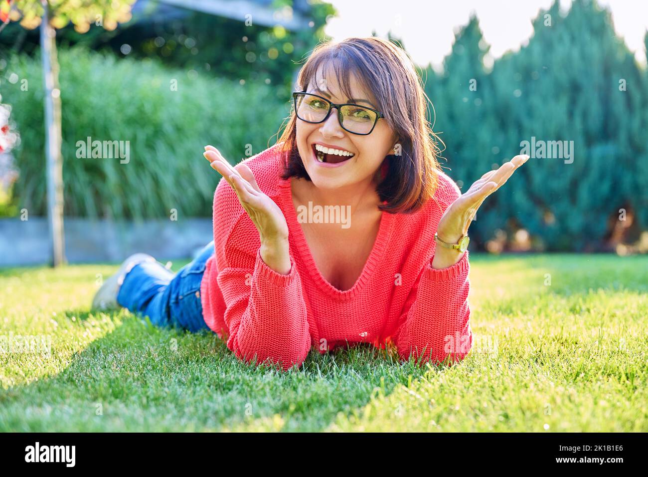 Outdoor Portrait Of Smiling Middle Aged Woman Lying On Grass Stock