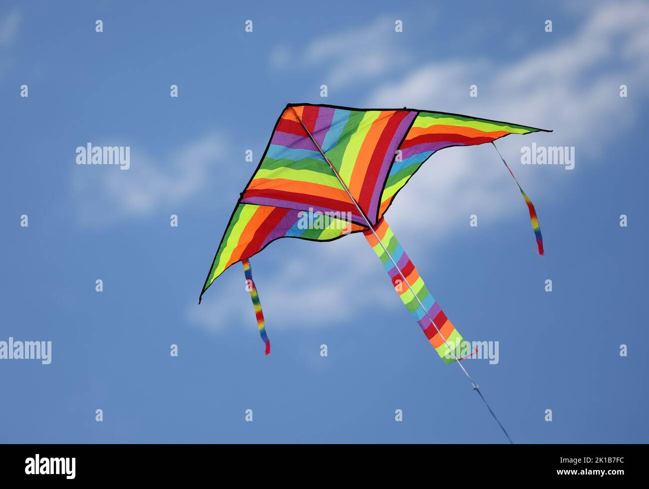 large kite with the many colors of the rainbow flying high attached to ...