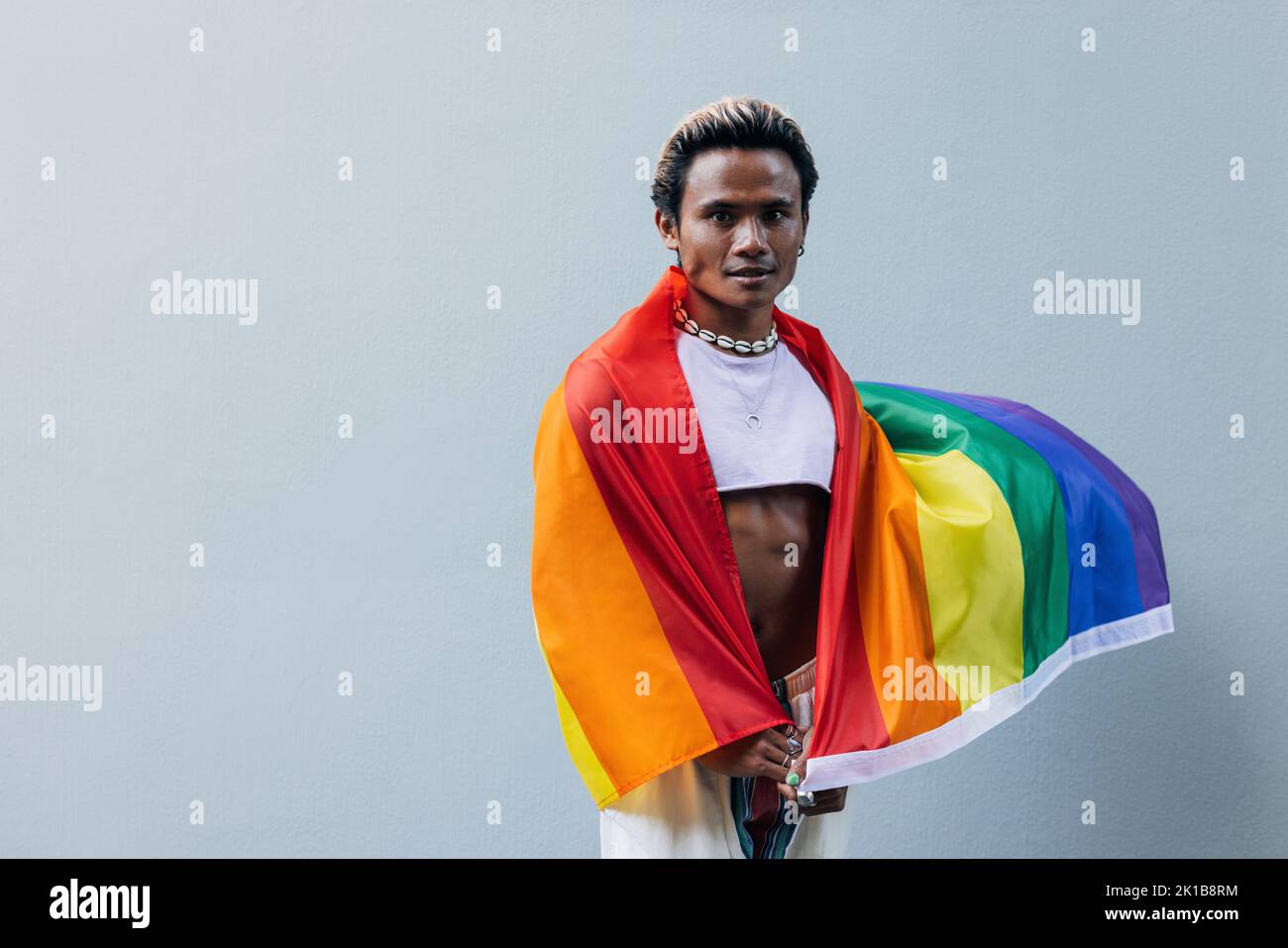 Portrait of a young guy with lgbt flag posing outdoors at grey wall ...