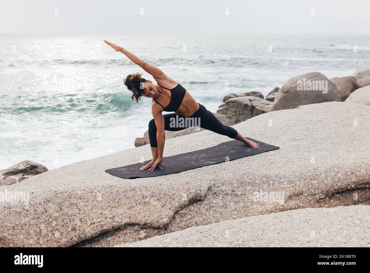Woman practicing Extended Side Angle Pose by ocean at sunset Stock ...