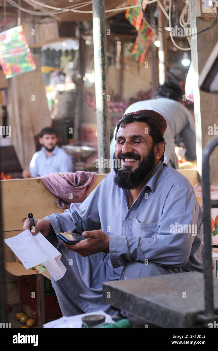A vertical shot of a Pakistani male with a beard in a market doing ...