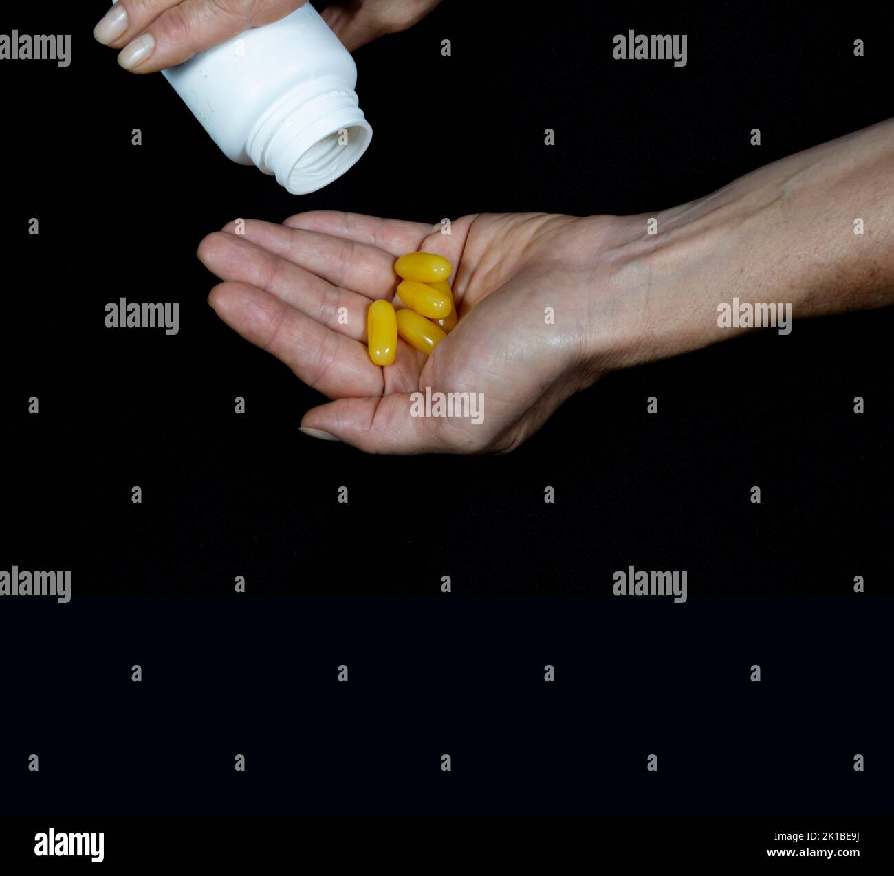 One hand pours yellow pills into the palm of another hand against a ...